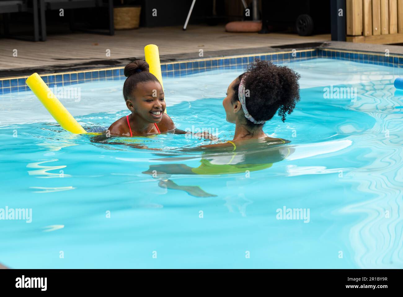 Happy african american mother teaching daughter to swim with float in ...