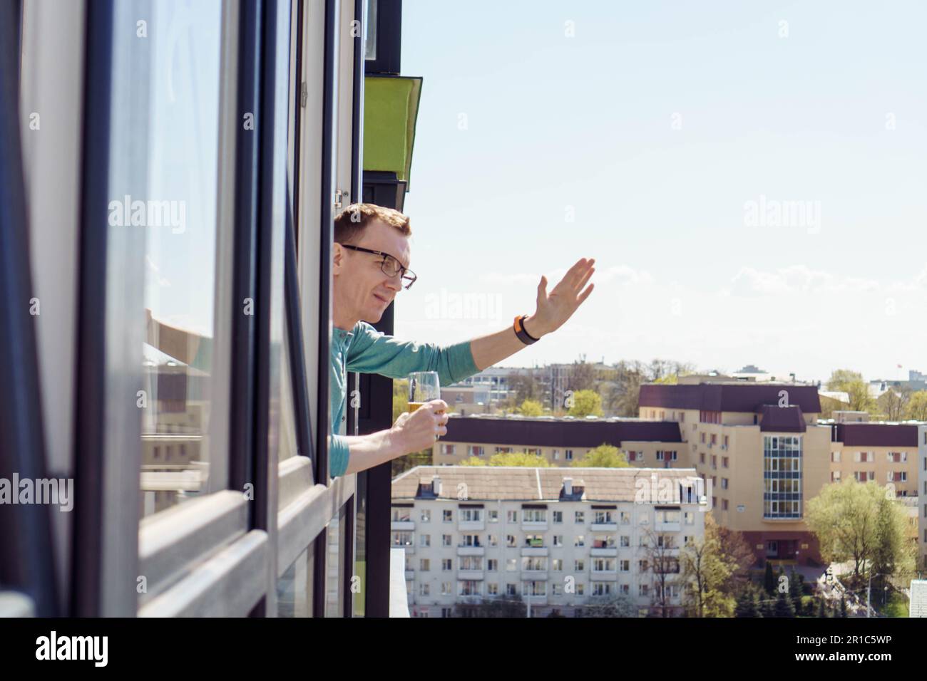 Man with glass of juice, beer, drink looks out of apartment window ...