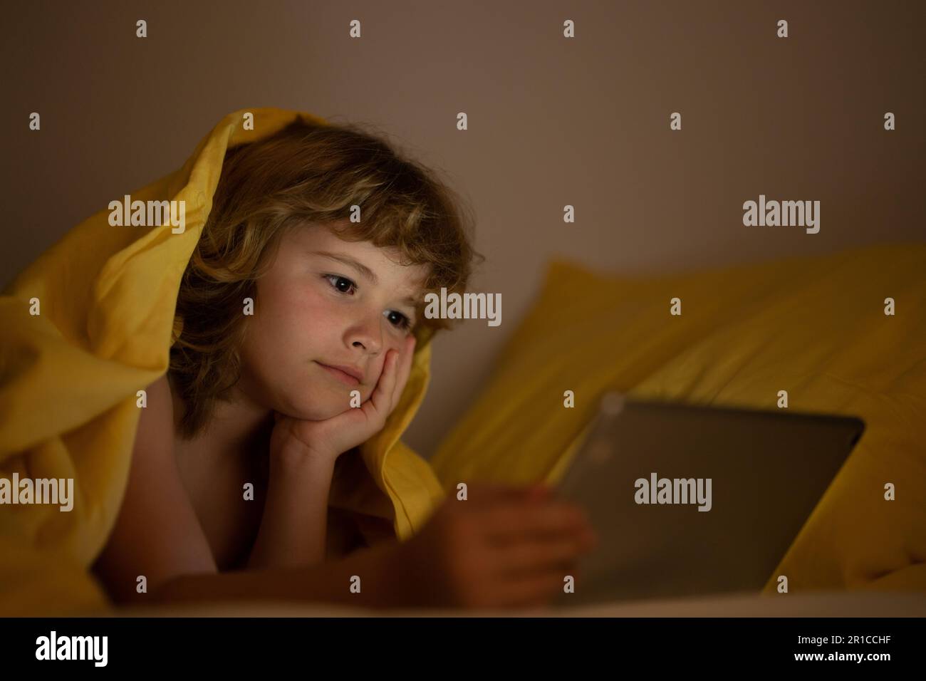 Kid alone at home. Kid lying in bed at night and playing digital tablet ...