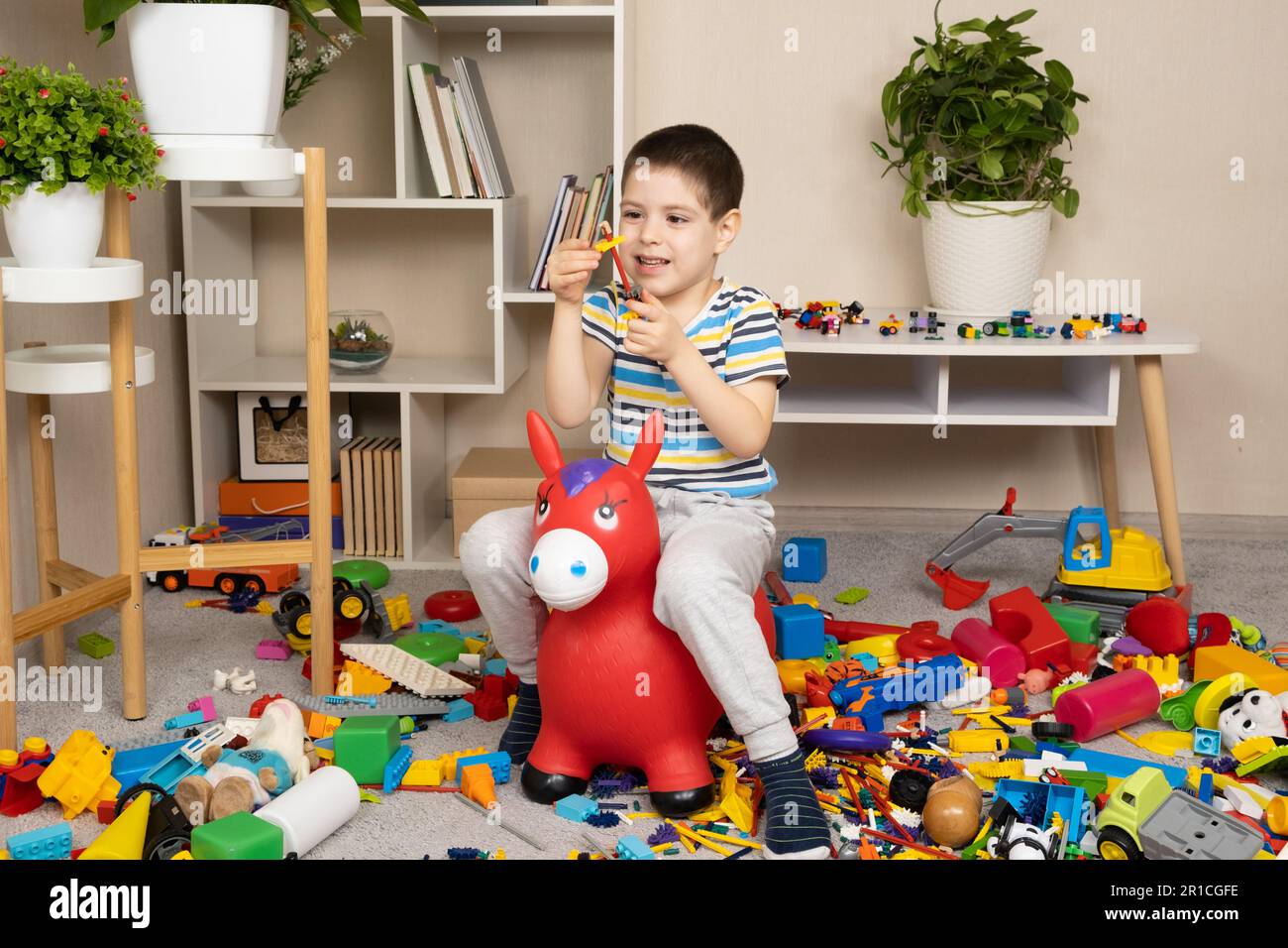 A little boy is jumping on an inflatable rubber donkey among the mess ...