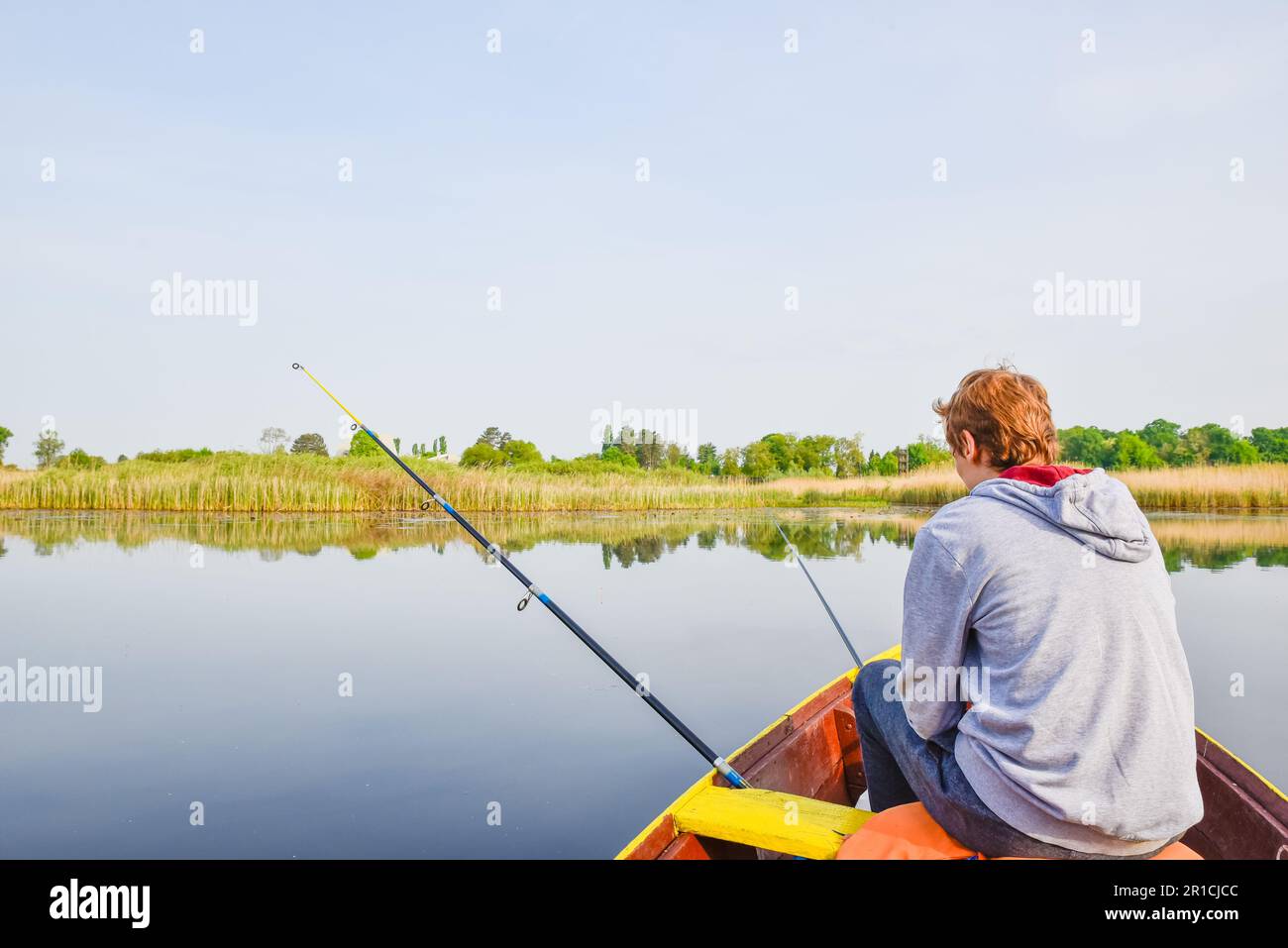 Boy Sitting in Fishing Boat on Tranquil Lake Holding a Rod in a Scenic ...