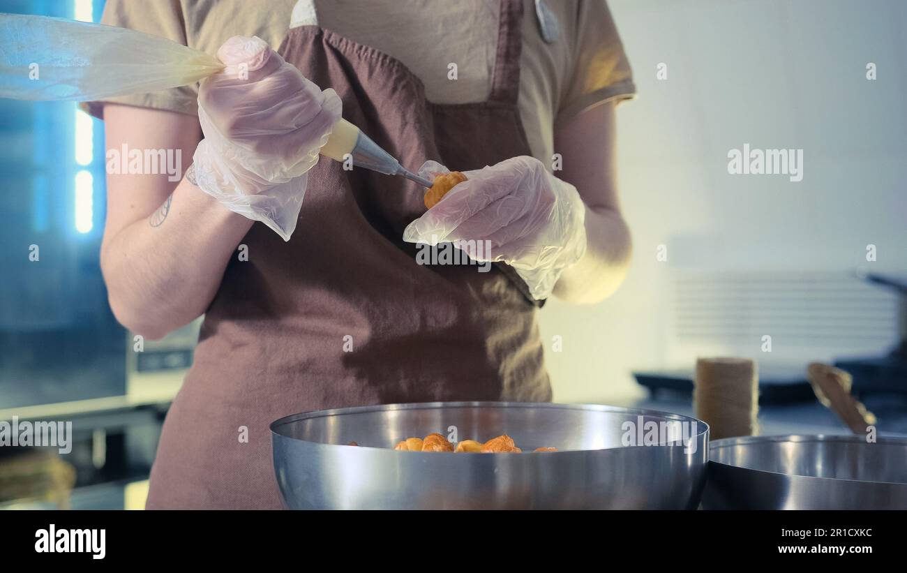 a female pastry chef in the kitchen fills custard cakes with butter ...