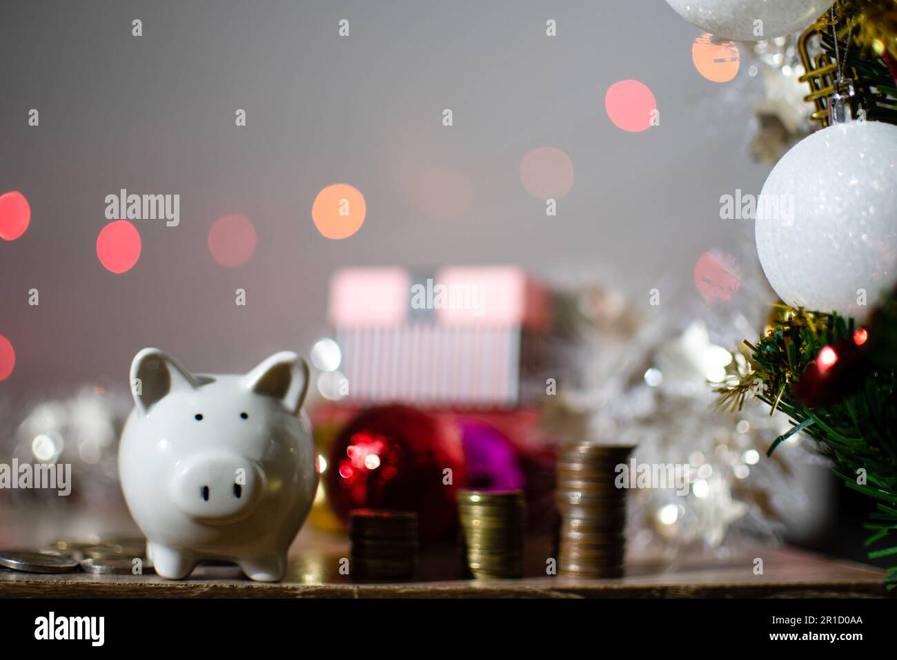 Closeup, White piggy banks, many coins on table wooden. Green Christmas tree decorated with ...
