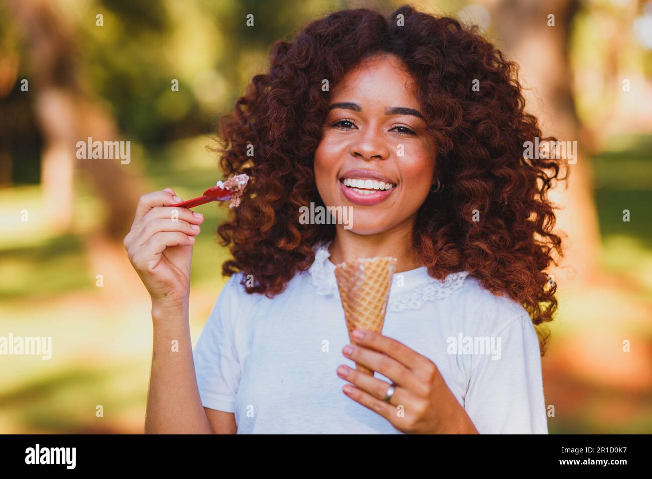 Happy afro woman eating ice cream in the park Stock Photo - Alamy