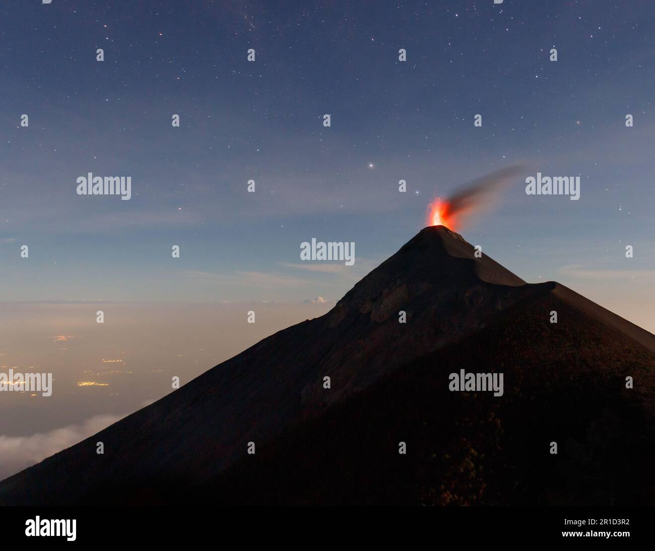 Volcano fuego lava eruption at night with visible stars and city lights ...