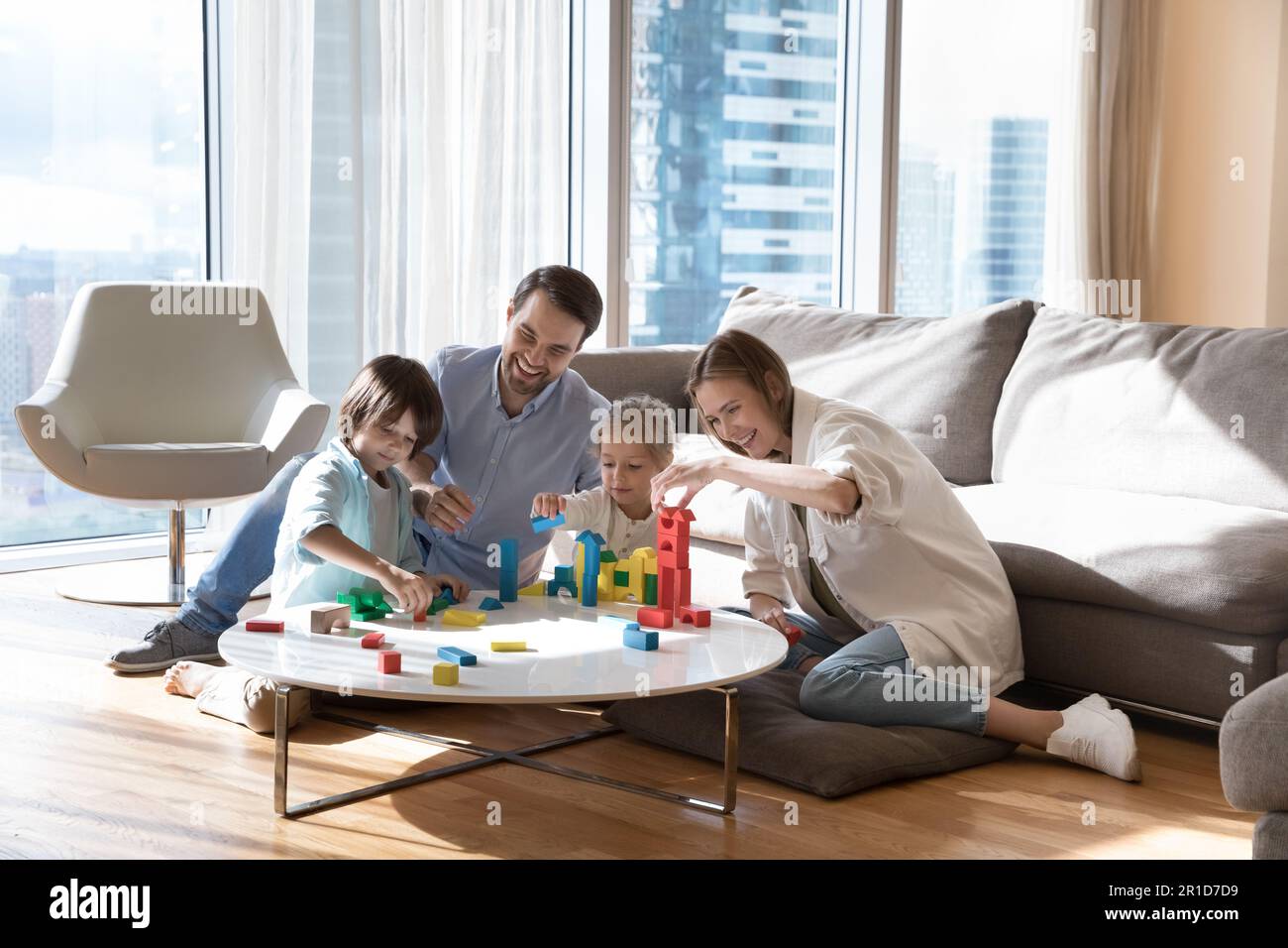 Happy positive parents and two little sibling children building towers ...