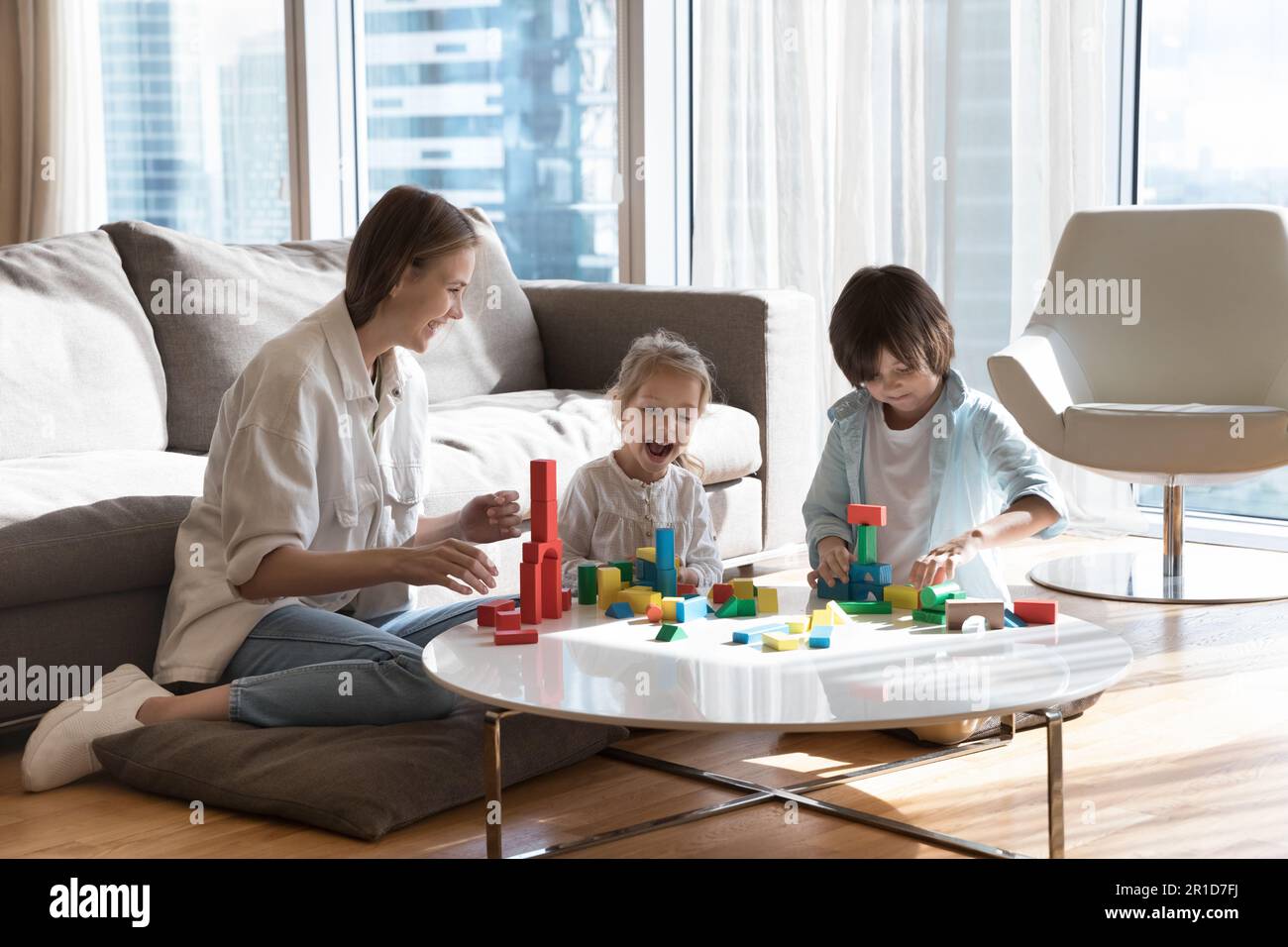 Happy mother helping little sibling kids to build toy towers Stock ...