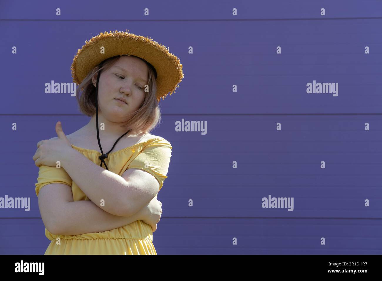 Upset Asian teen girl in a hat and dress hugs herself with her arms on ...