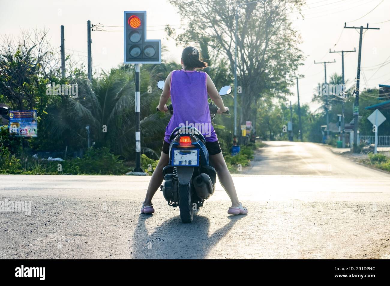 A woman with a motorcycle is standing at the rural intersection with ...
