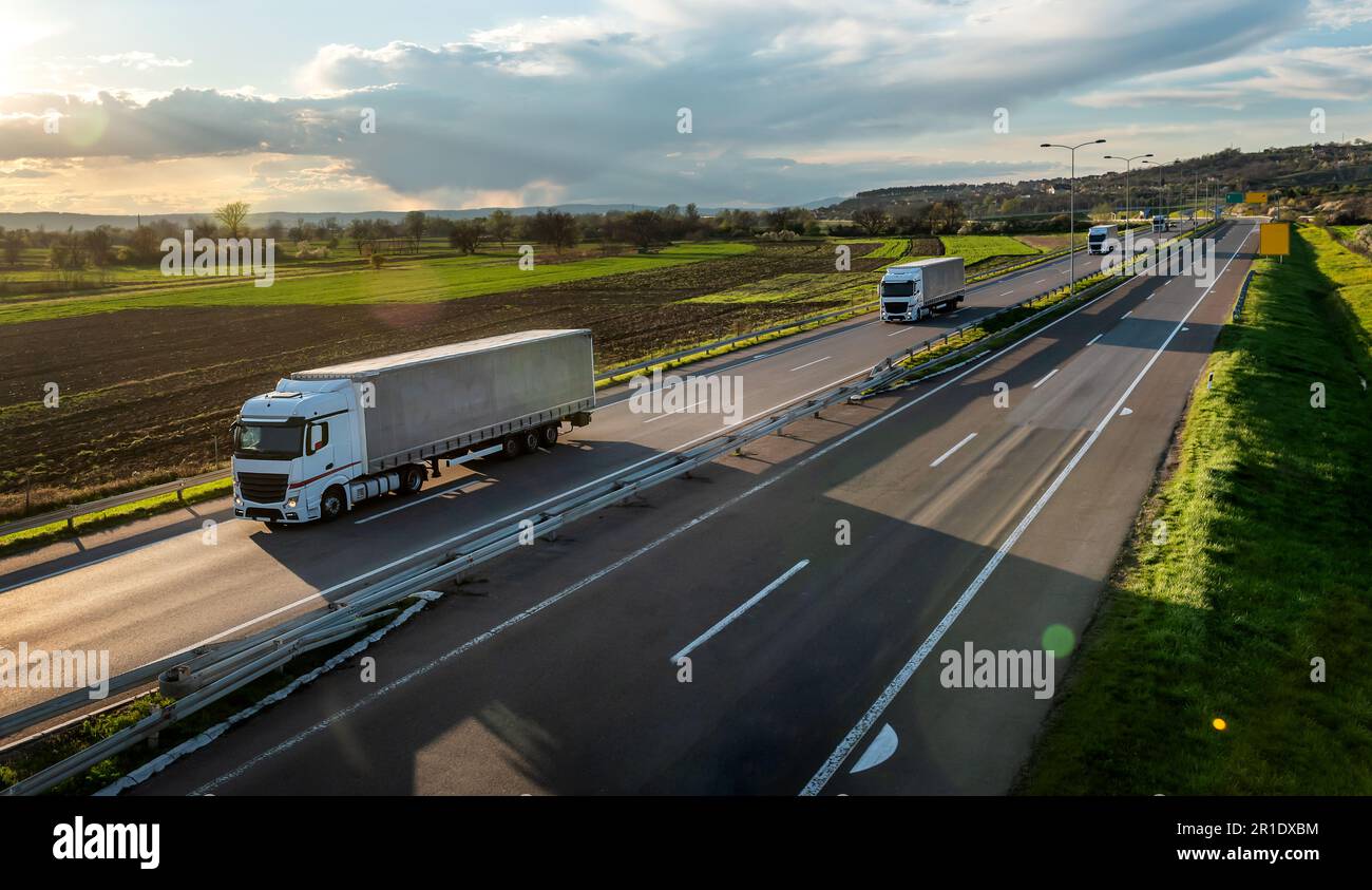 Convoy of white Trucks with containers on highway at bright sunset ...