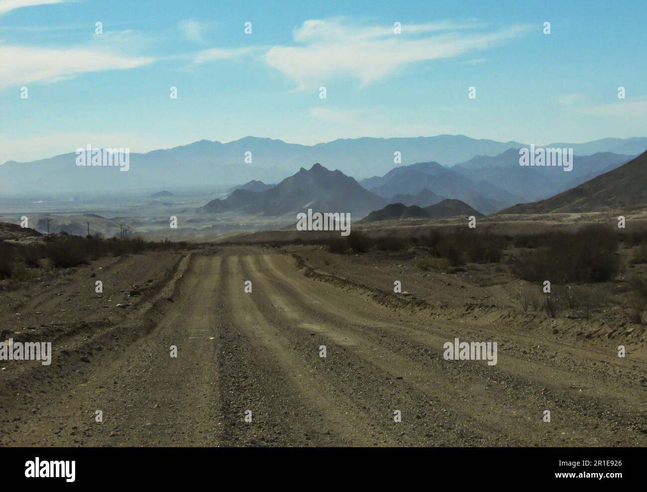 A Deserted dirt road leading towards the rugged distant blue mountains ...