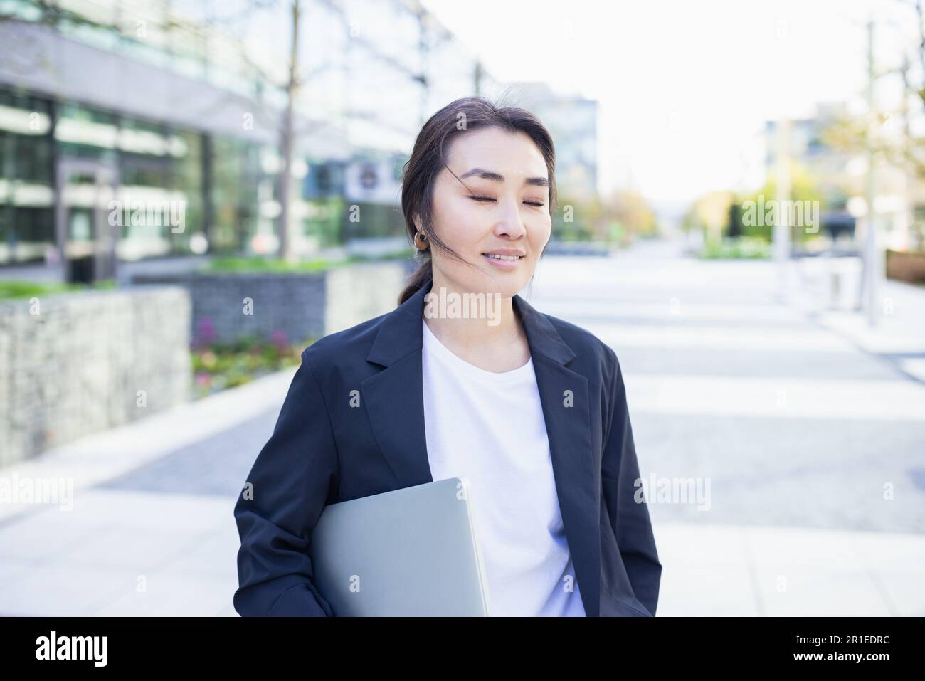 Relaxed and confident Asian business woman in suit holding laptop ...
