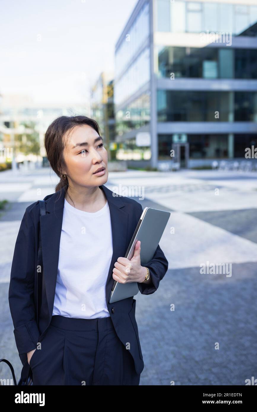 Relaxed and confident Asian business woman in suit holding laptop ...