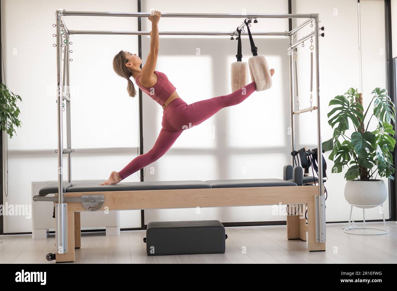 Beautiful asian woman in pink sportswear doing pilates on bed reformer ...