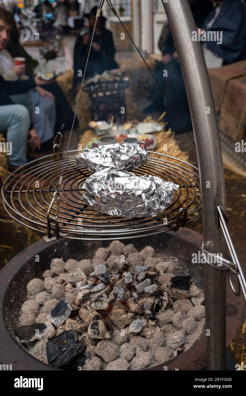 Potato in alumnium foil baked on charcoal barbecue grill outdoor in ...