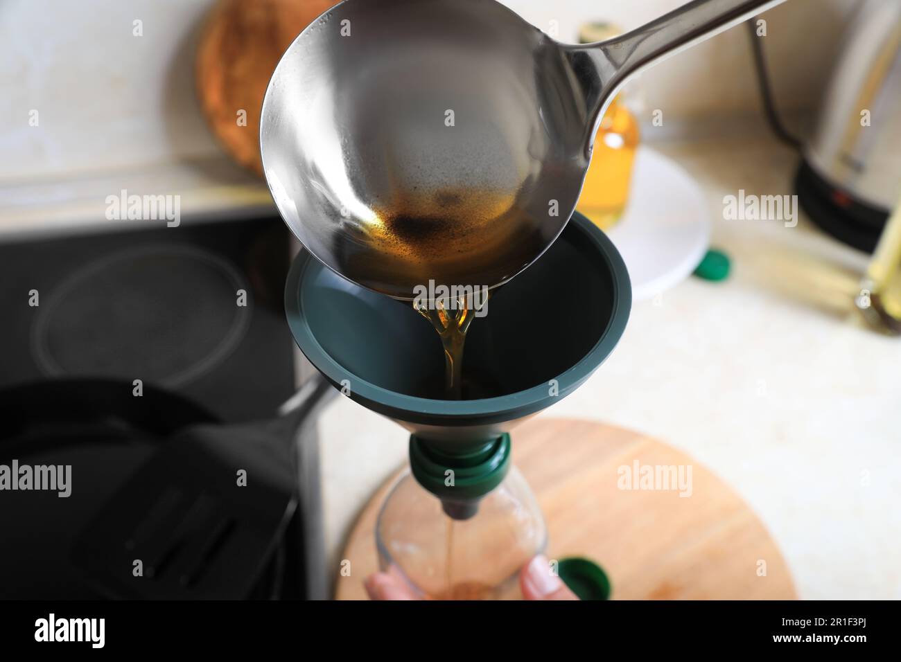 Woman pouring used cooking oil into bottle through funnel in kitchen ...