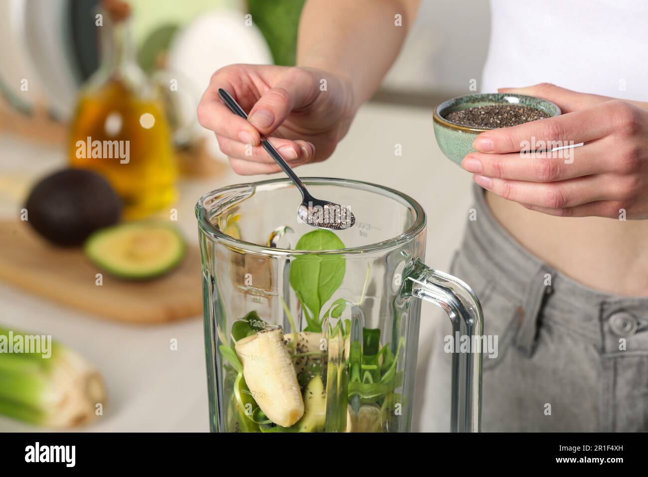 Woman adding chia seeds into blender with ingredients for green ...
