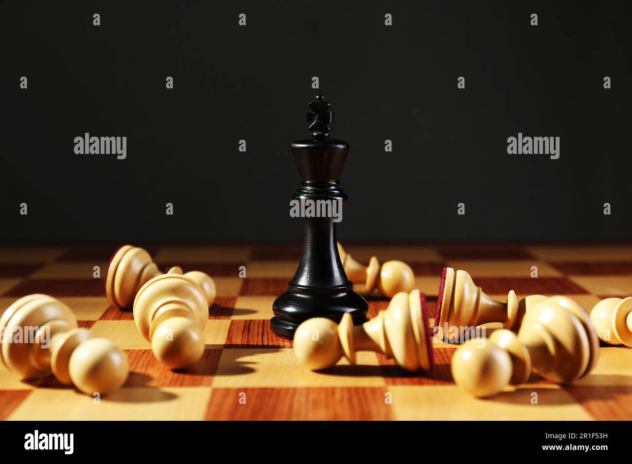 King among fallen white chess pieces on wooden board against dark ...