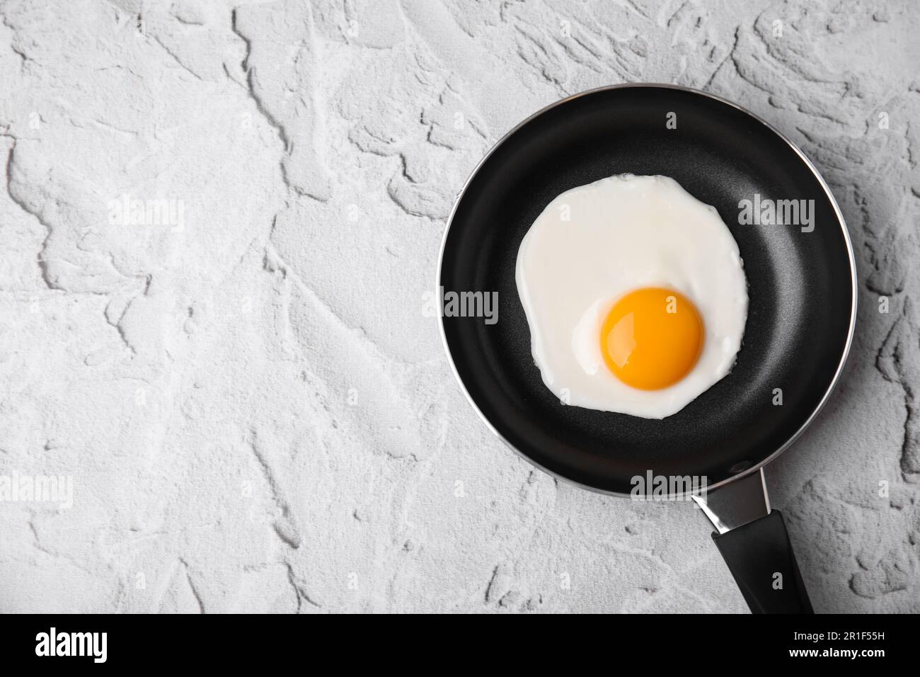 Tasty fried egg in pan on white textured table, top view. Space for ...