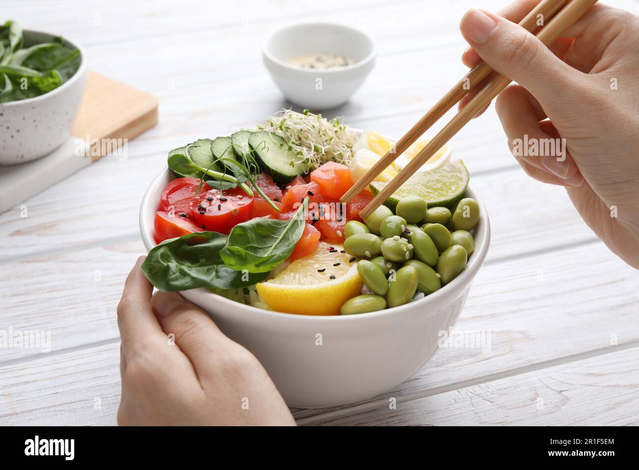 Woman eating delicious poke bowl with quail eggs, fish and edamame ...