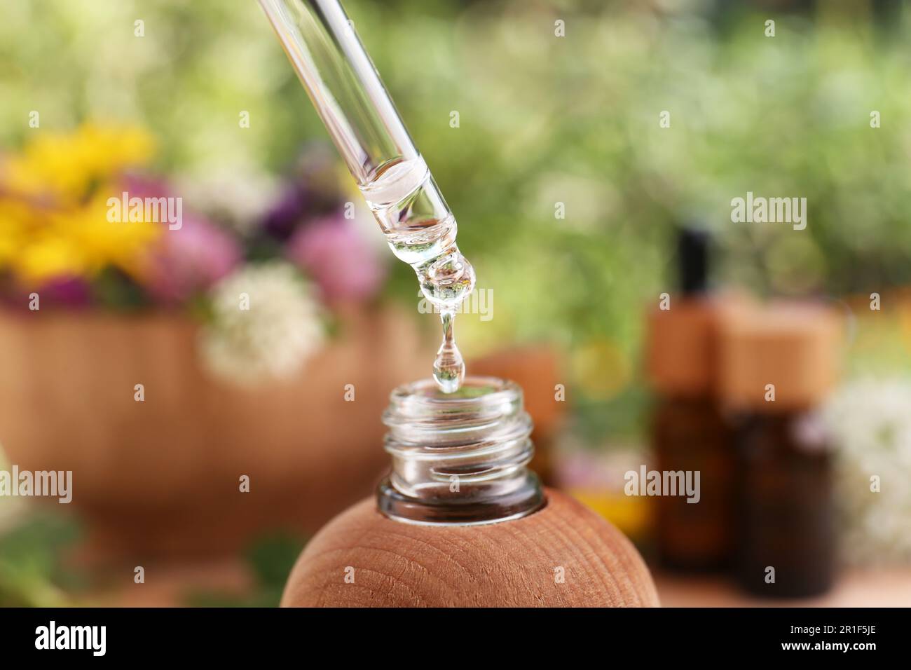 Dripping essential oil from pipette into bottle on blurred background ...