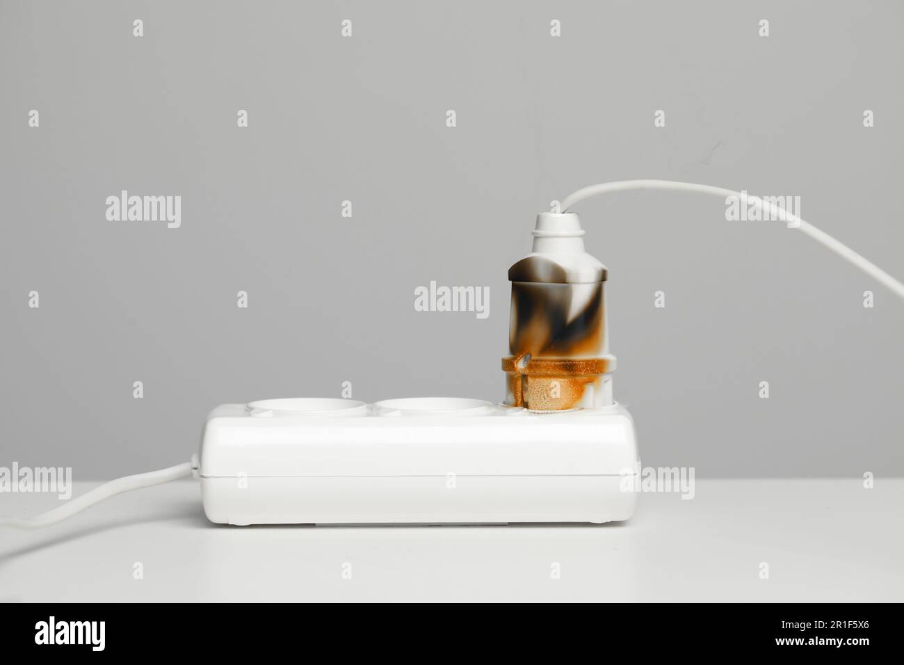 Inflamed plug in power strip on white table against grey wall ...