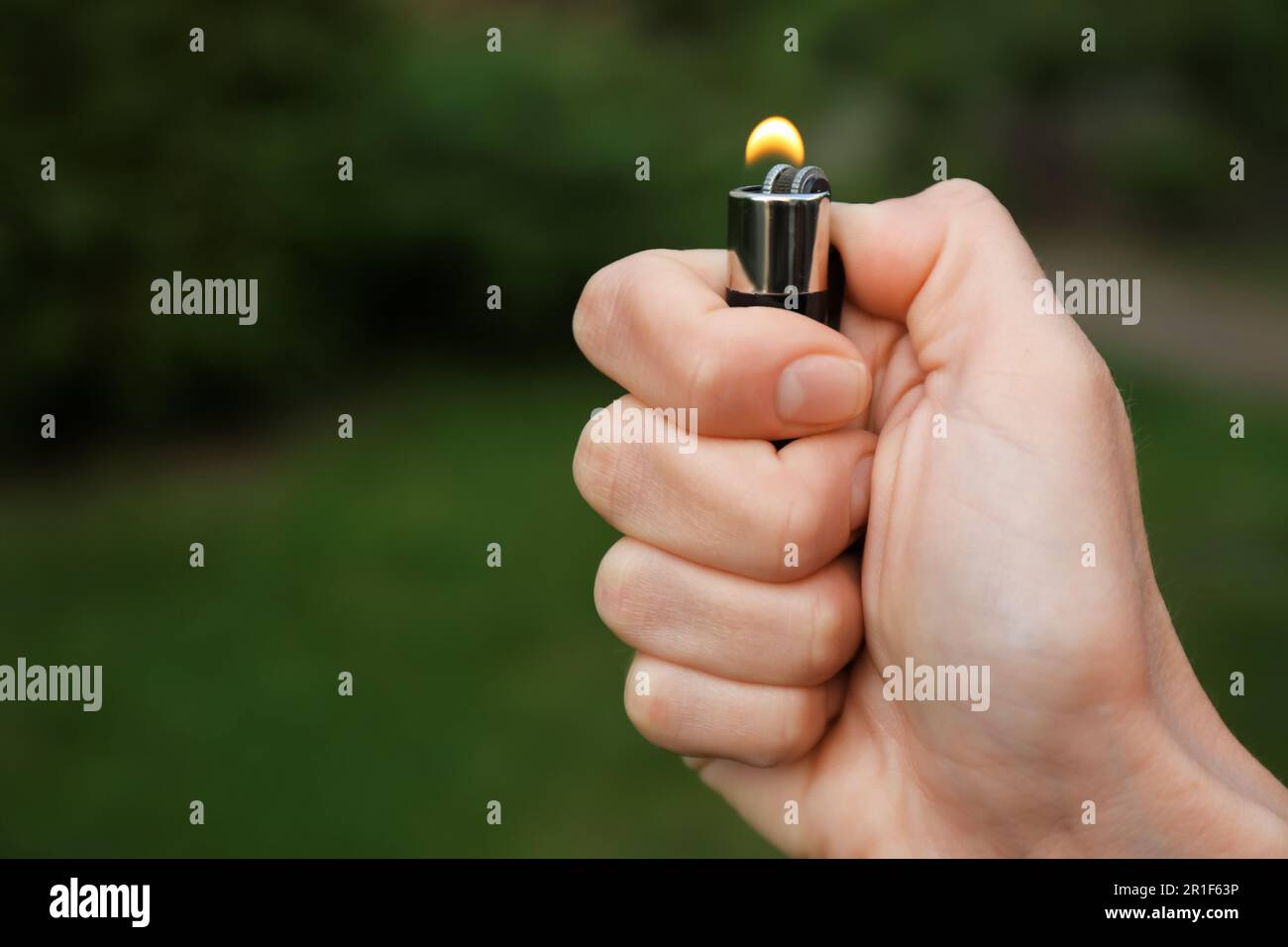 Man holding lighter with burning flame outdoors, closeup. Space for ...