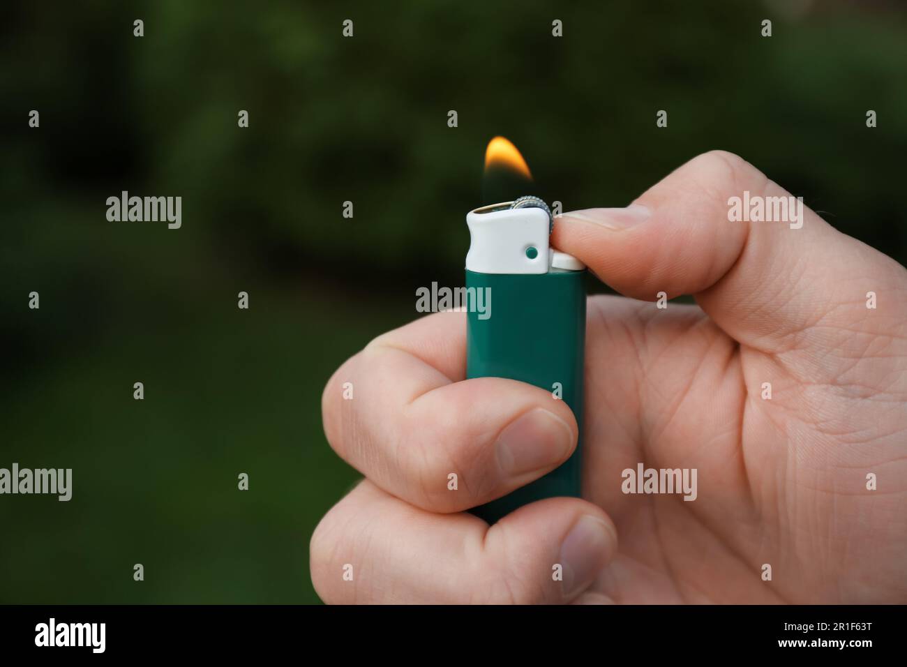 Man holding lighter with burning flame outdoors, closeup. Space for ...
