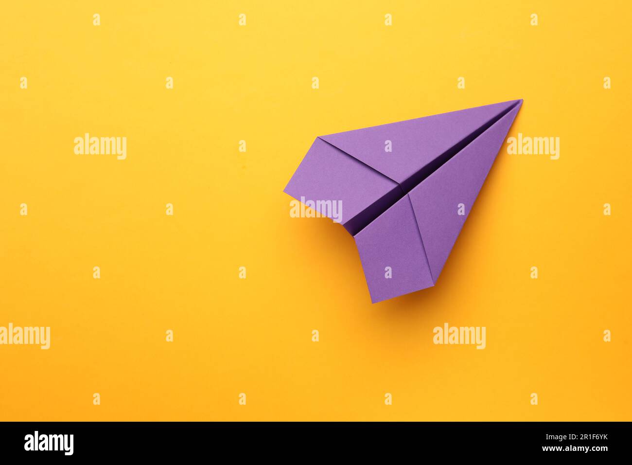 Handmade purple paper plane on yellow background, top view. Space for ...