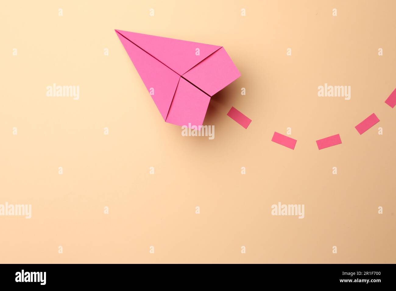 Handmade pink paper plane with dotted lines on beige background, top ...