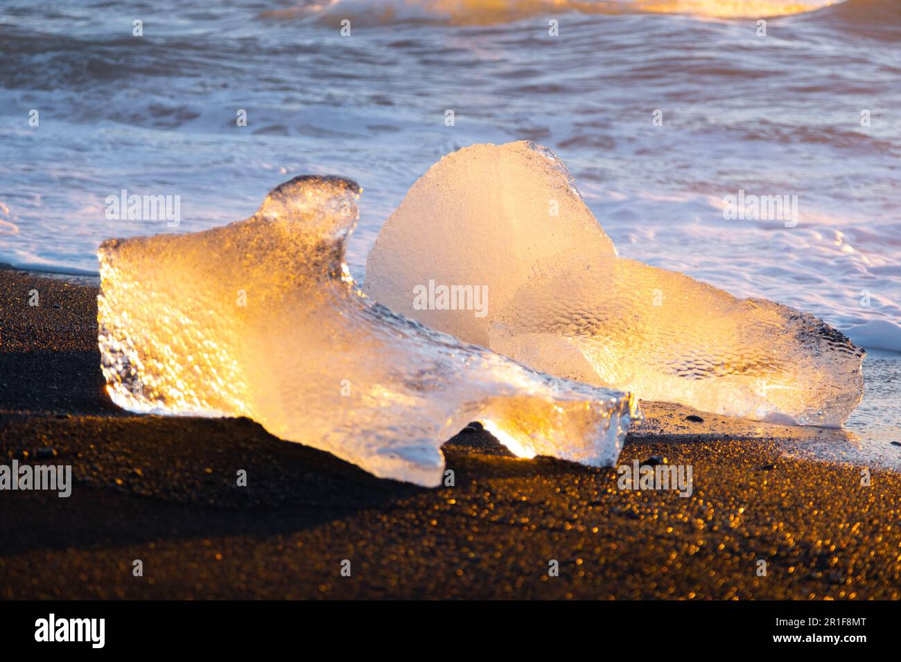 Pure glacier ice shining at sunset. Black volcanic sand at ocean coast ...