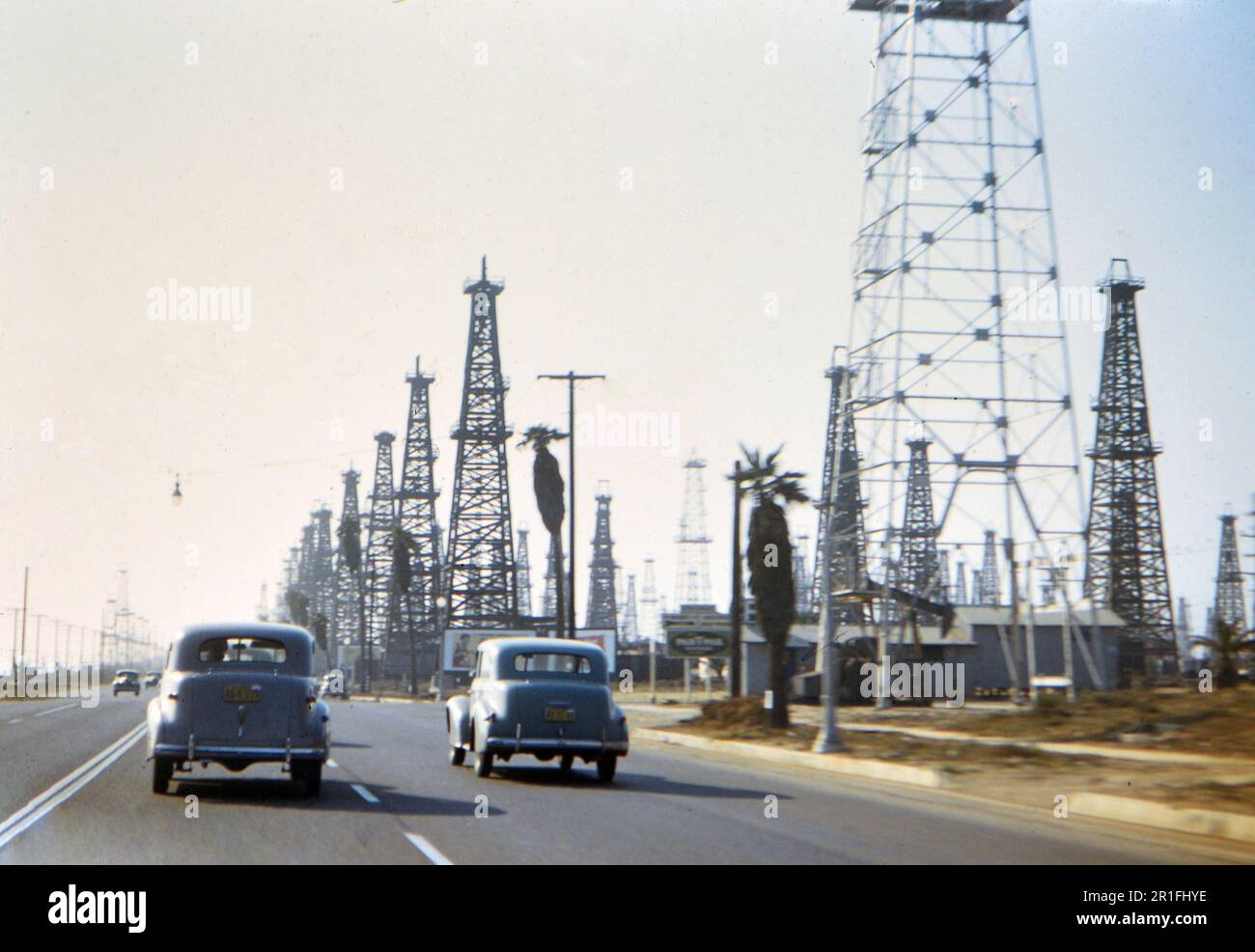 Cars driving down a highway in California pass a field of oil well ...