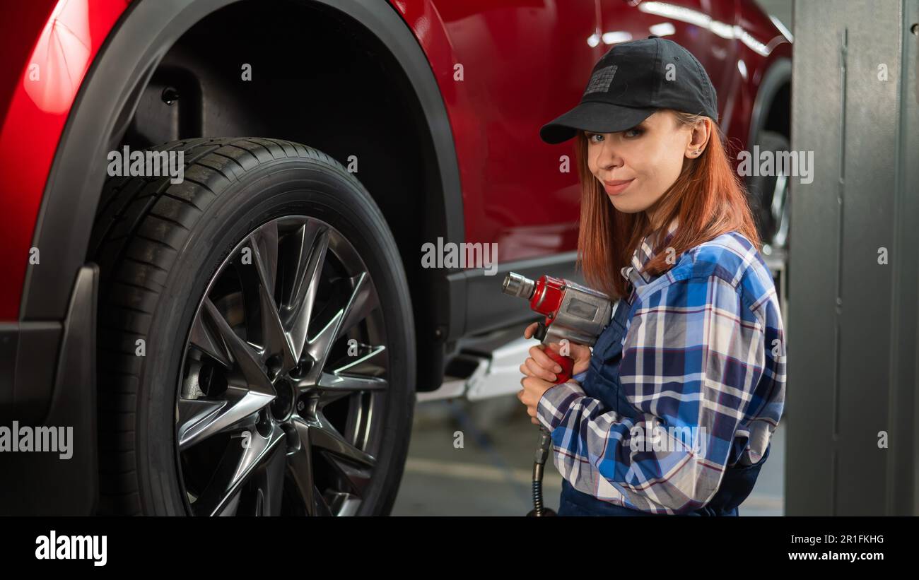 Woman mechanic uses pneumatic wrench to tighten the wheel nut. Girl at ...