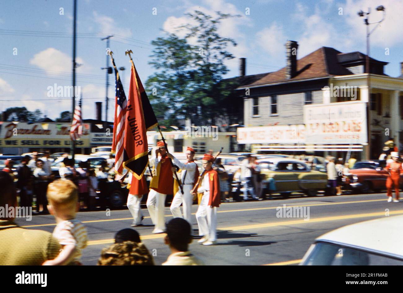 Color guard marching in a parade, a used car dealer in the background ...