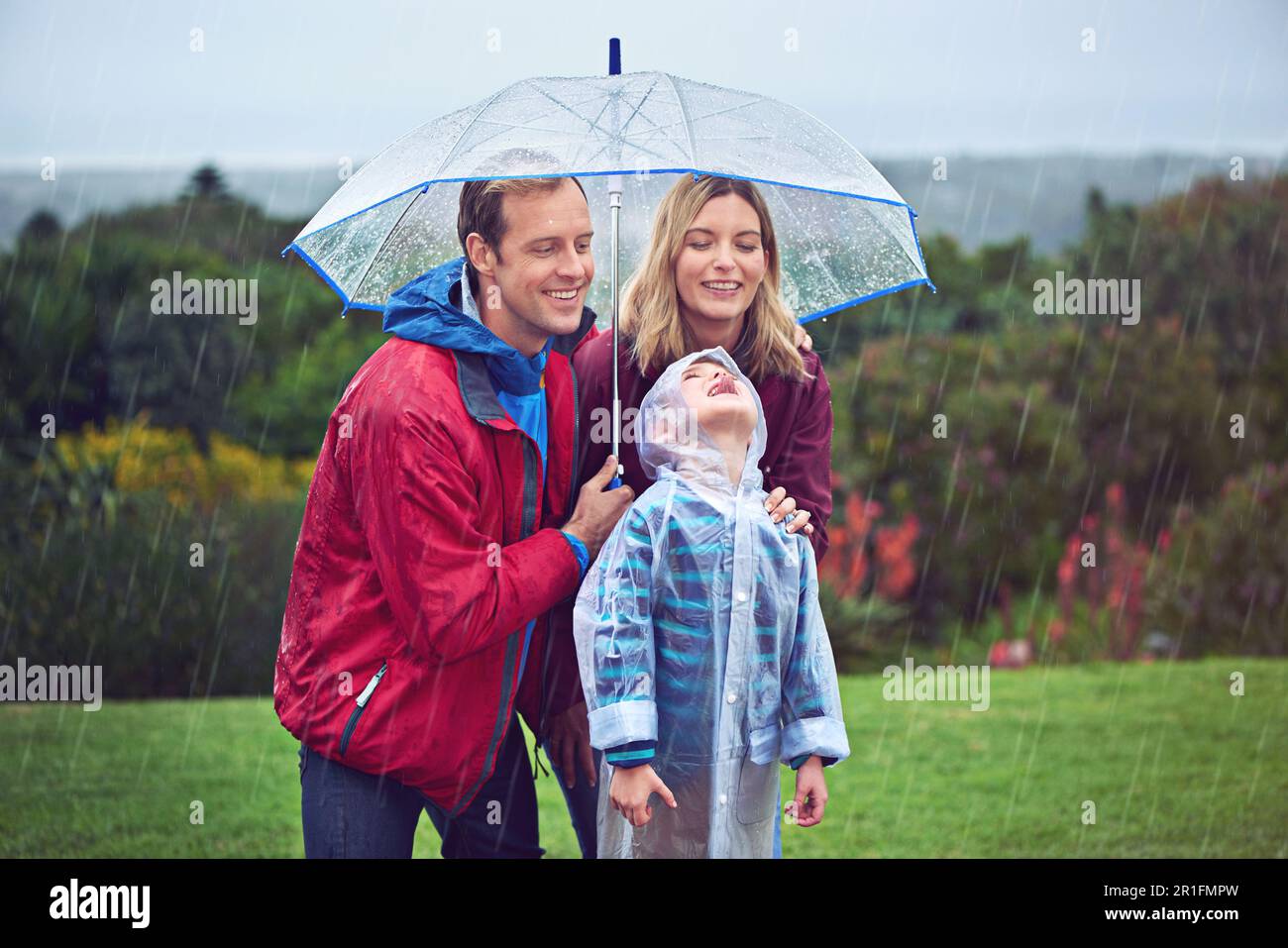 Family, happy and outdoor in rain with umbrella in nature for fun ...