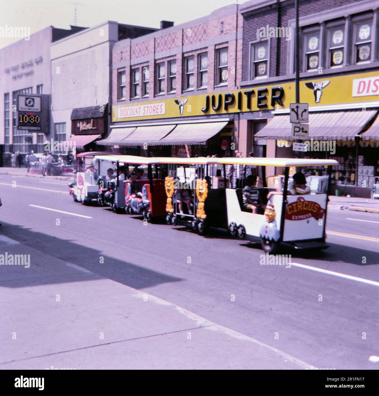 Kids riding a mini-circus train down the main street of a city in the ...