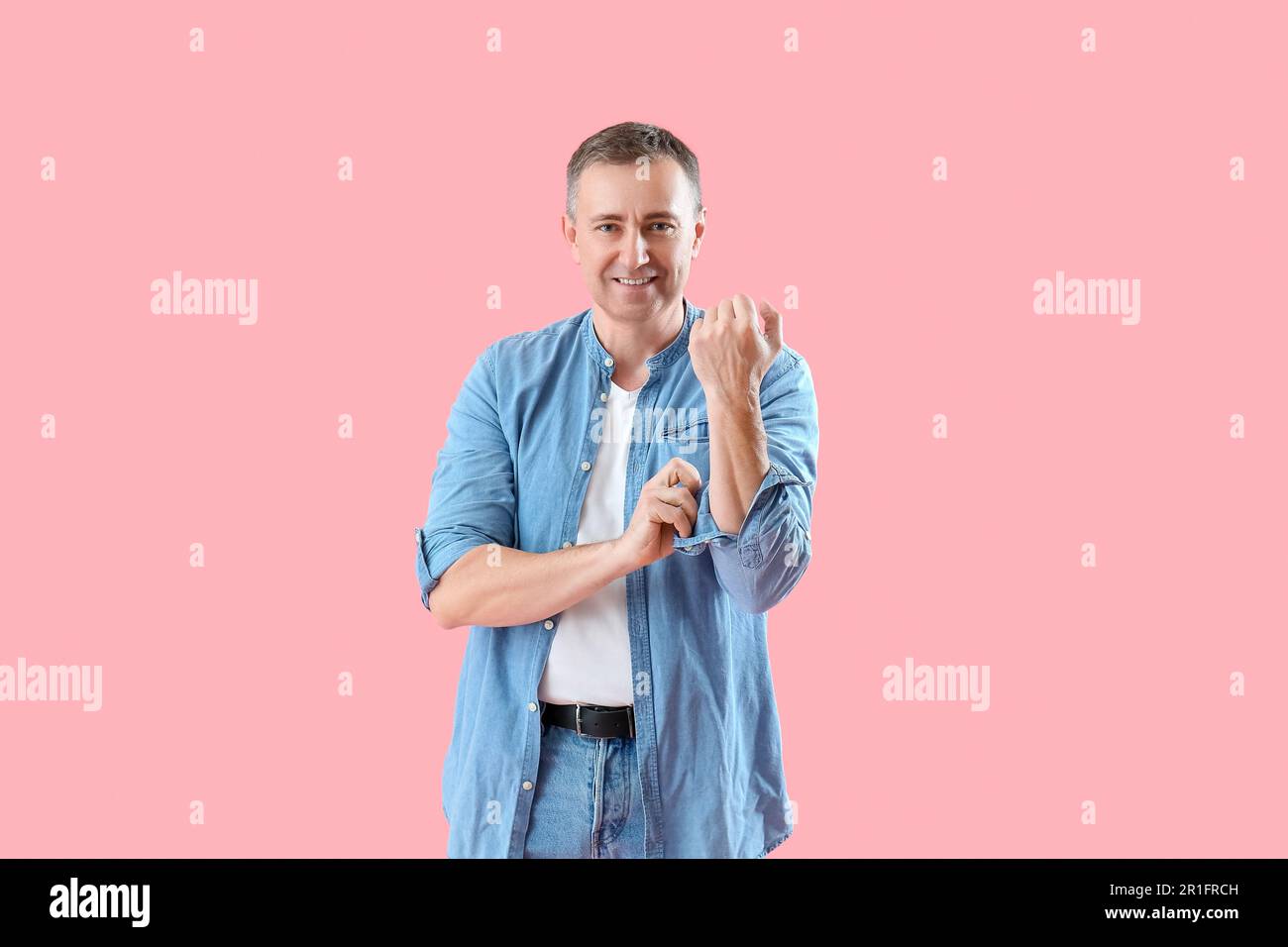Mature man rolling up his sleeve on pink background Stock Photo - Alamy