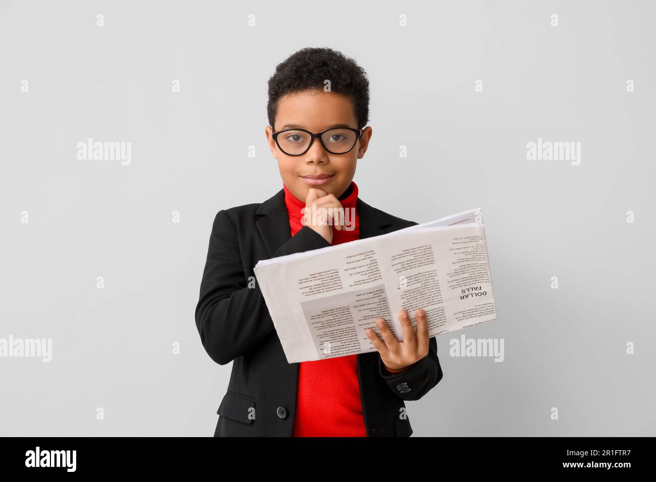 Little African-American boy reading newspaper on light background ...