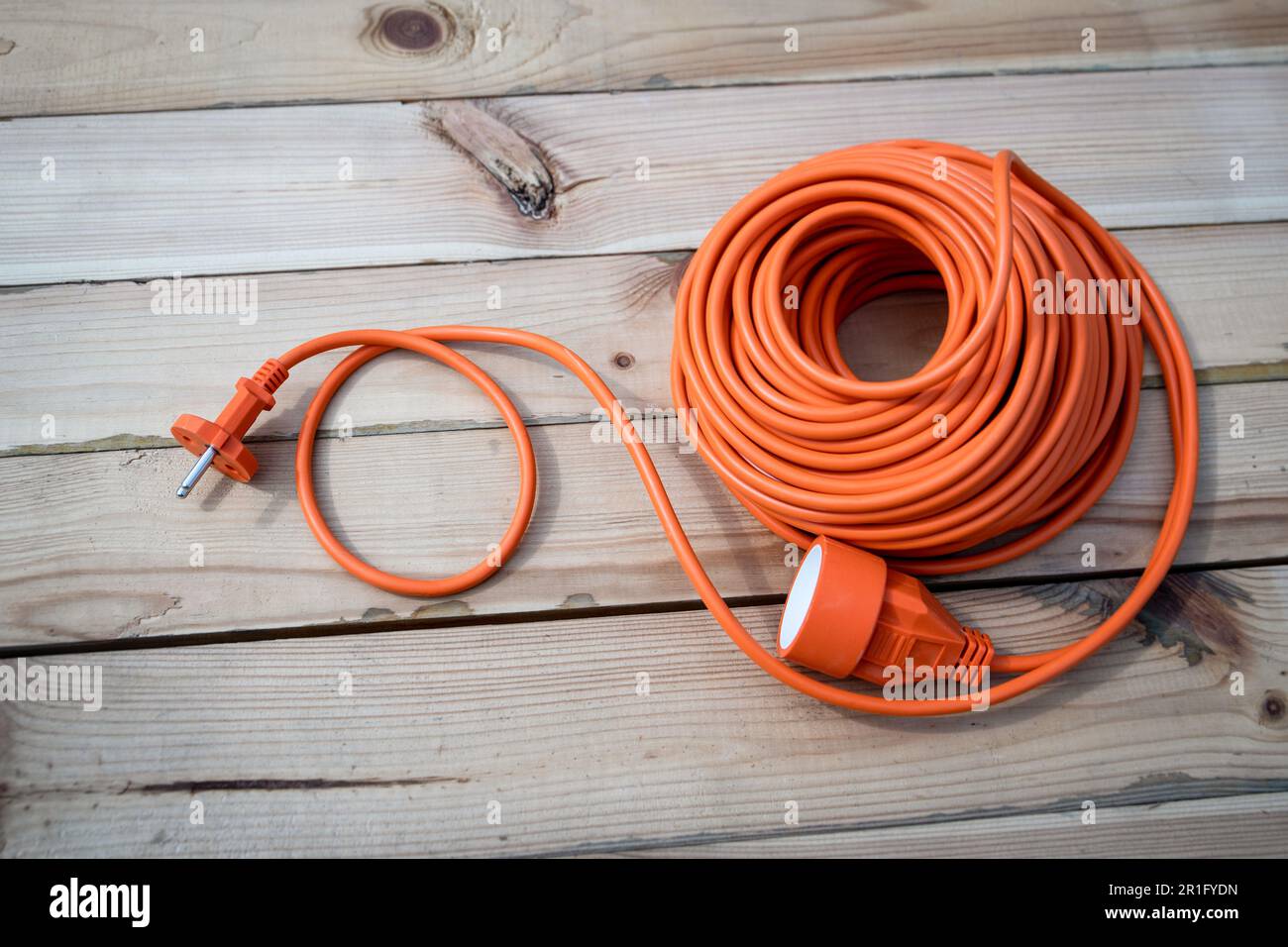 Orange construction electrical extension cord coiled on wood texture ...