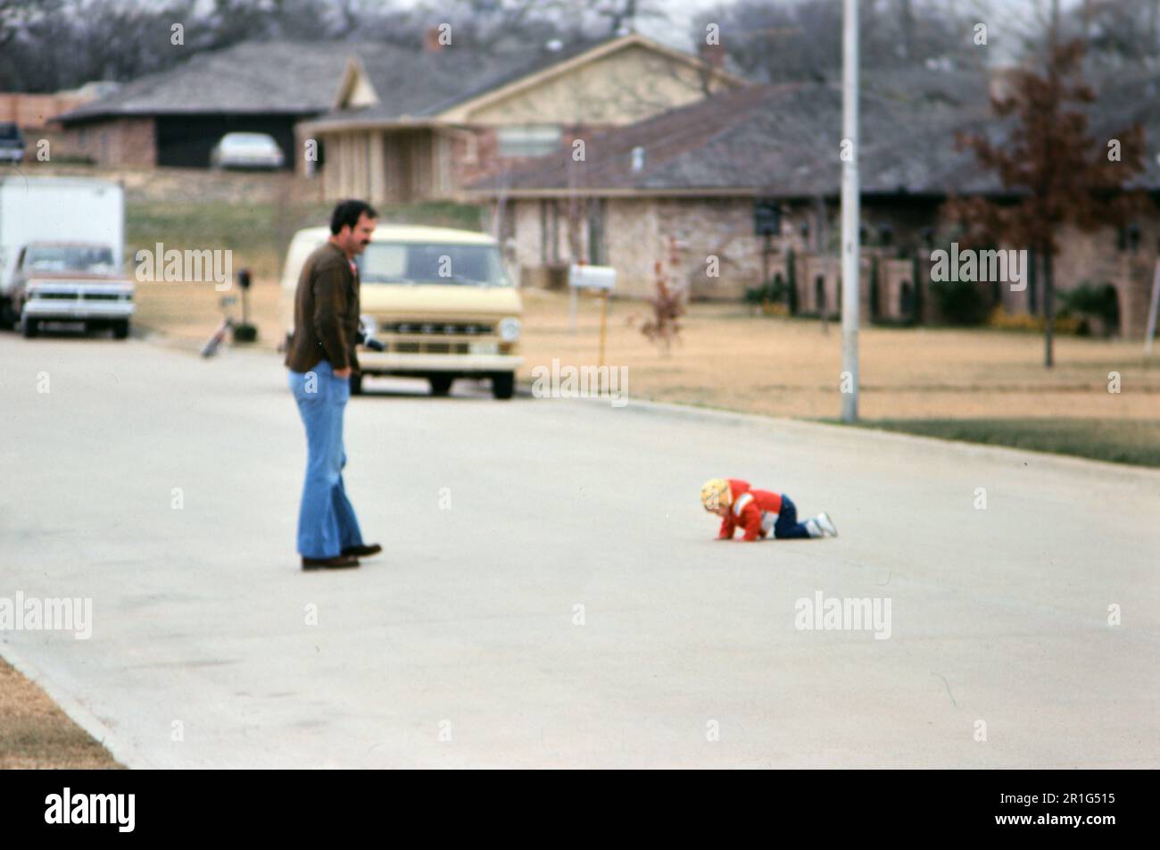 Father watching his infant child crawl in the middle of a street in a ...