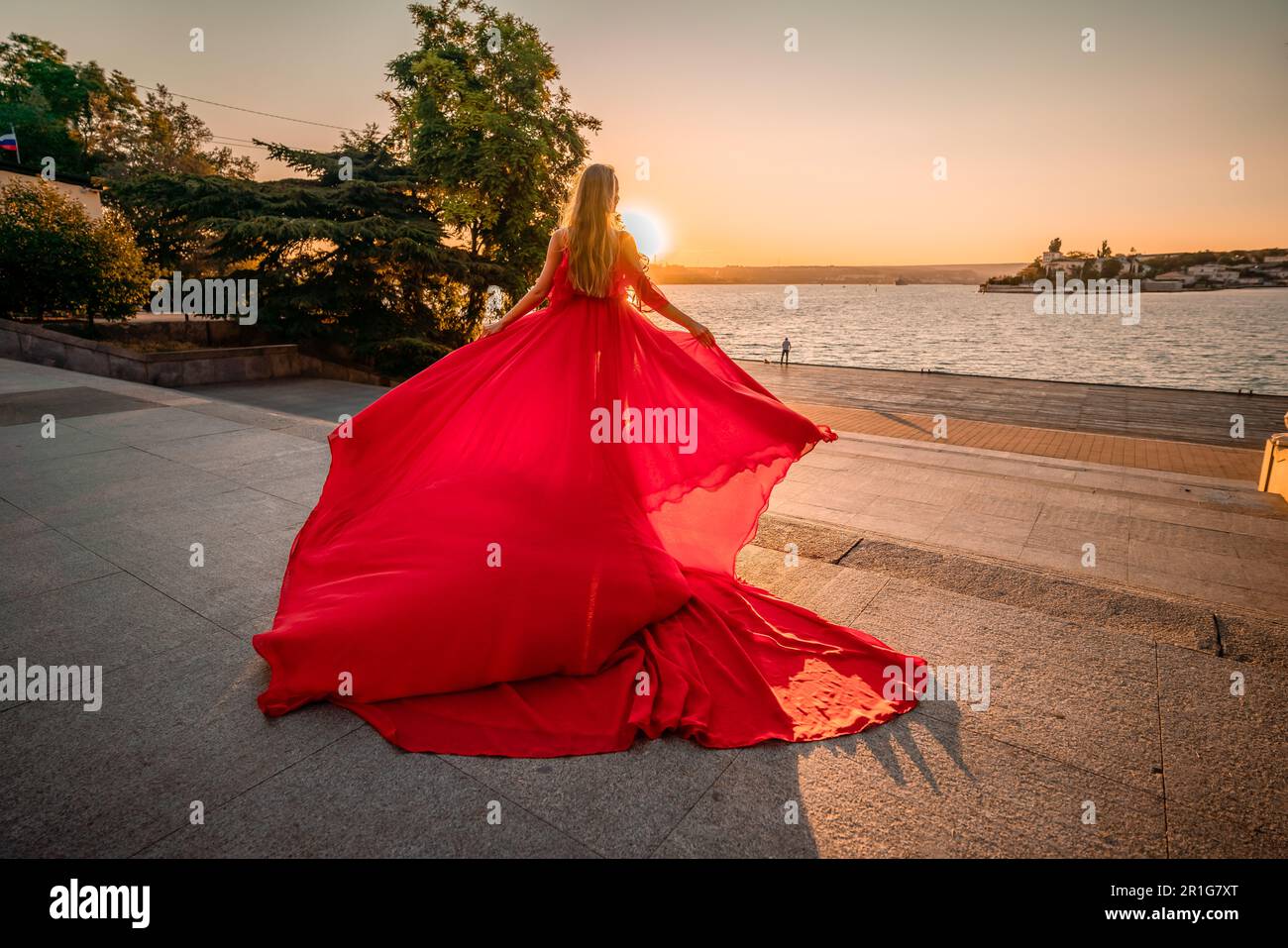 Sunrise red dress. A woman in a long red dress against the backdrop of ...