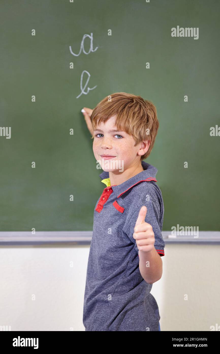 Portrait, child and student with thumbs up on blackboard in classroom ...