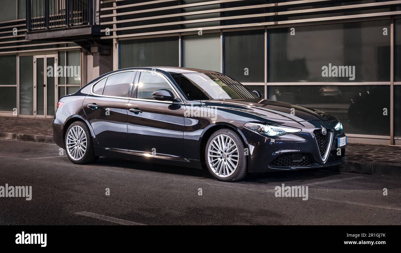 A silver Alfa Romeo automobile parked alongside a concrete building and ...