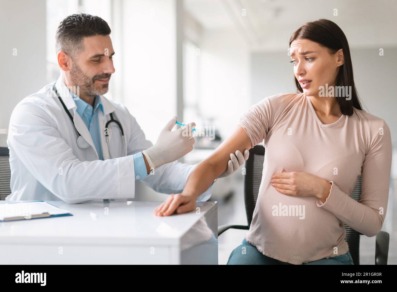 Young pregnant woman scared of vaccine injection, looking at syringe ...