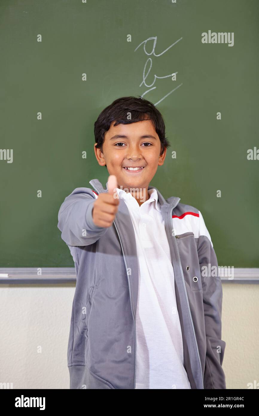 Portrait, child and thumbs up of student on chalkboard in classroom ...