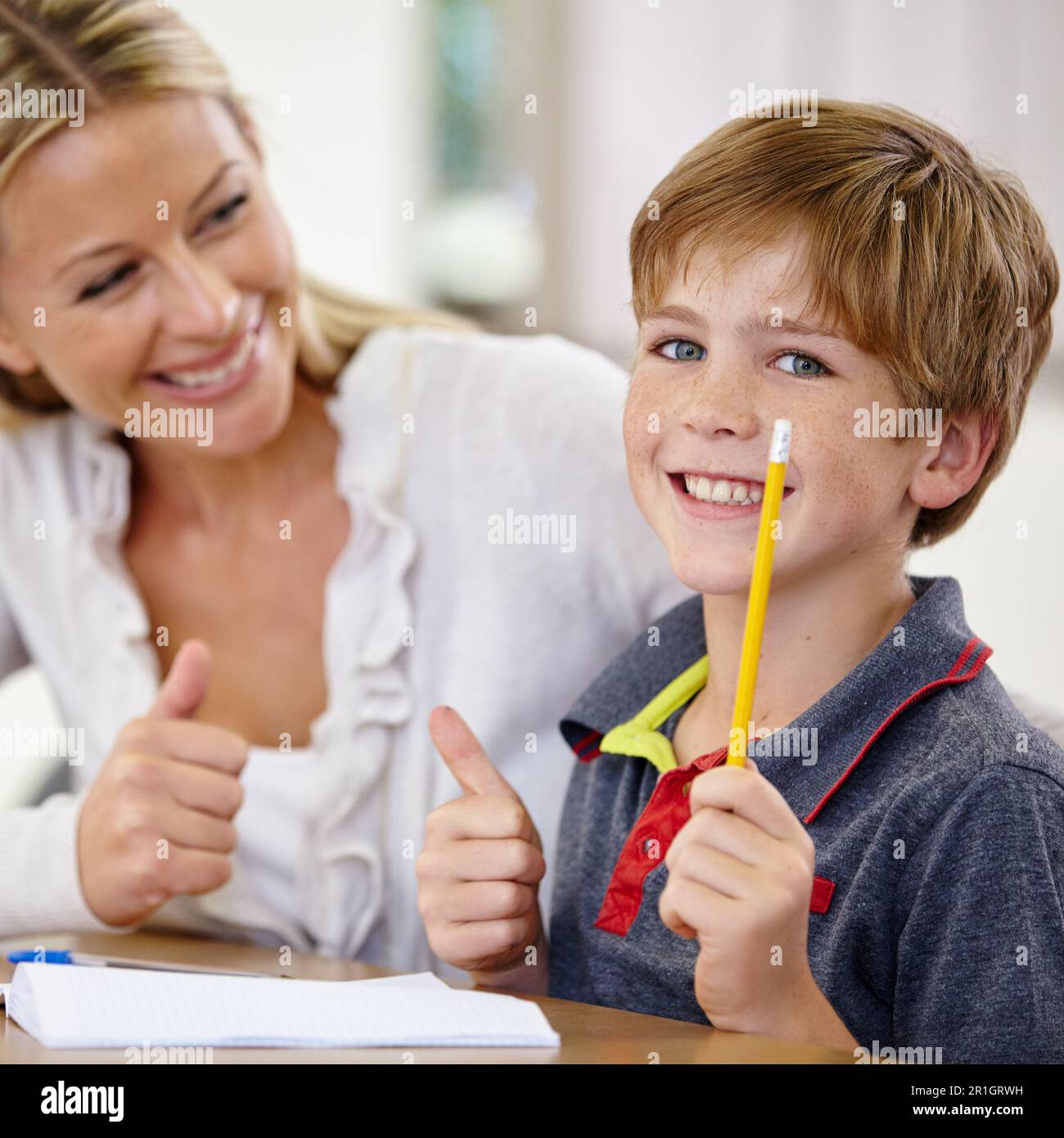Portrait, kid and teacher with thumbs up in classroom, smile and pencil ...