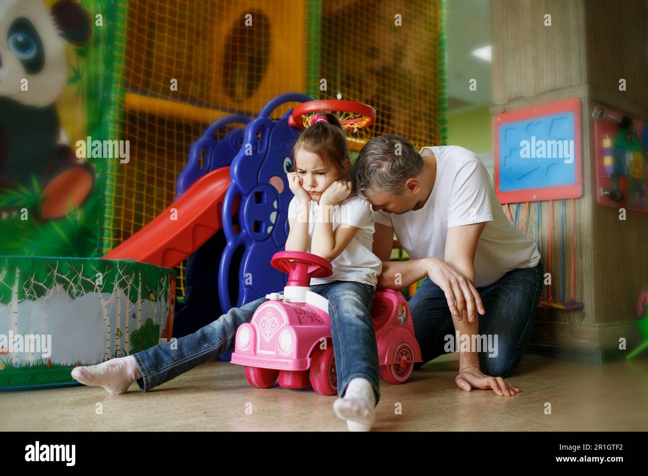 father and daughter are tired and sad sitting in the children's play ...