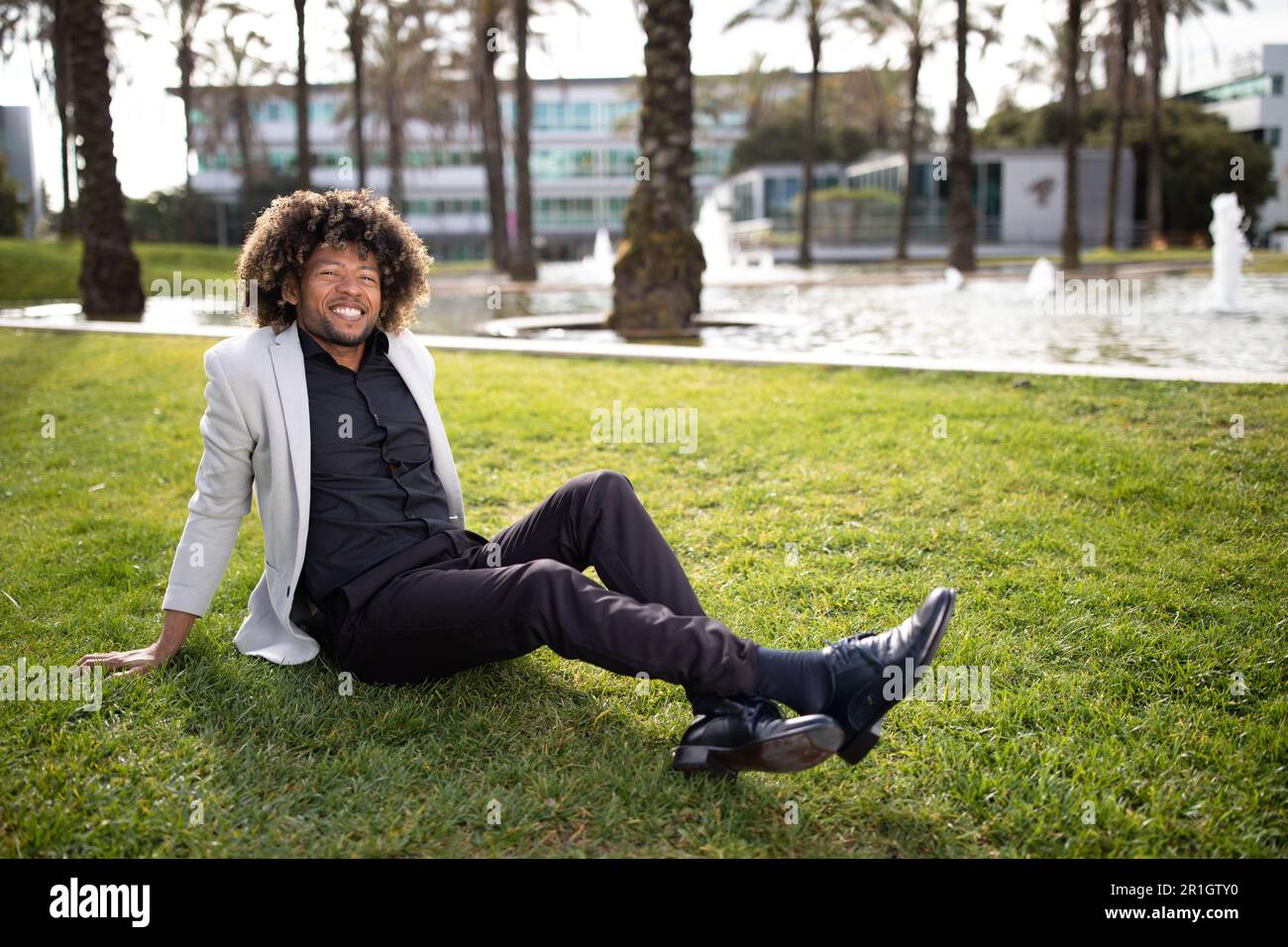 Happy black middle aged businessman sitting on grass in park, having ...