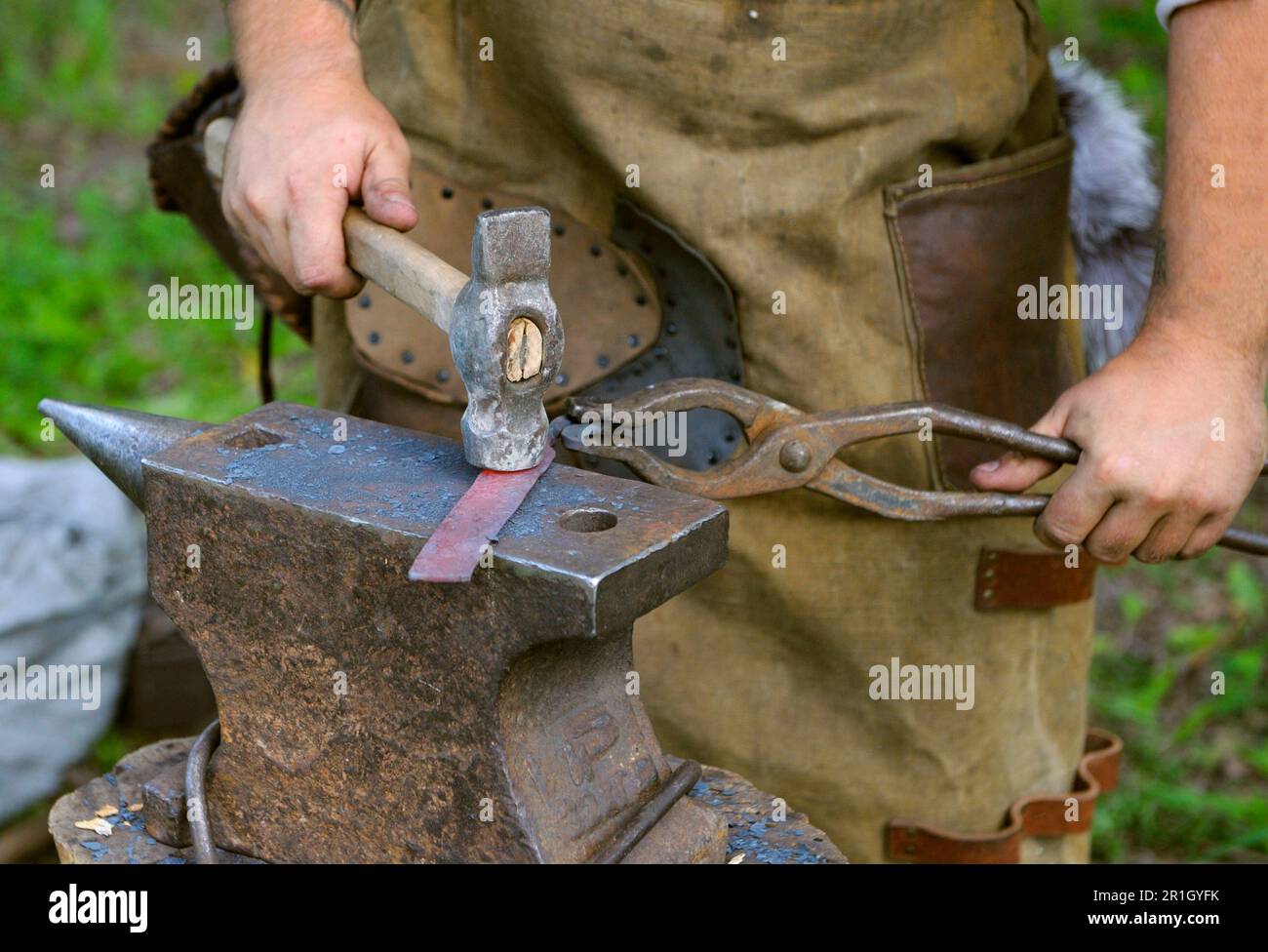 Blacksmiths hands holding forceps and hammer forging a metal billet ...