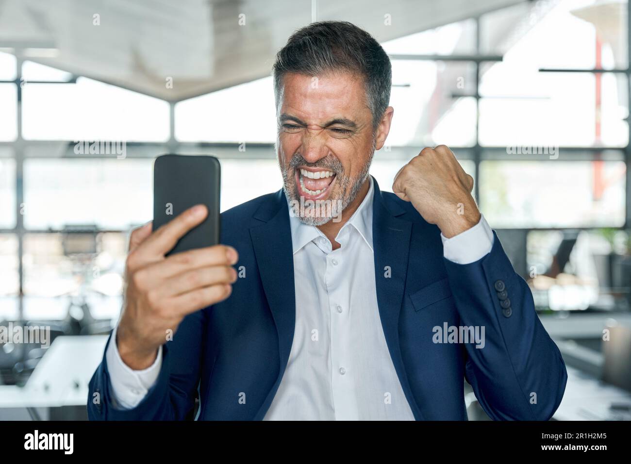 Happy mature business man looking at mobile phone celebrating success ...